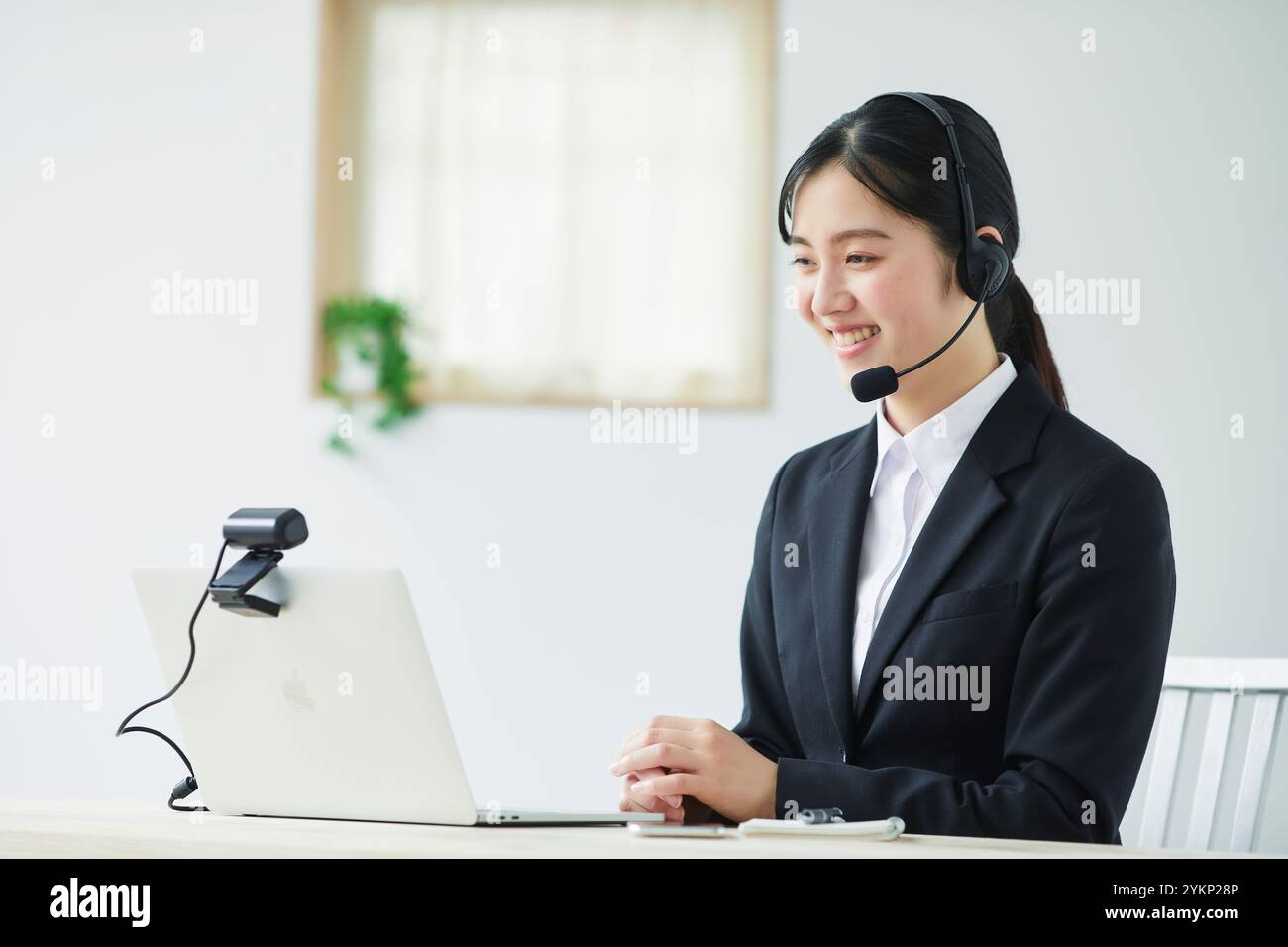 Young woman in smiling suit with intercom speaking into laptop camera ...