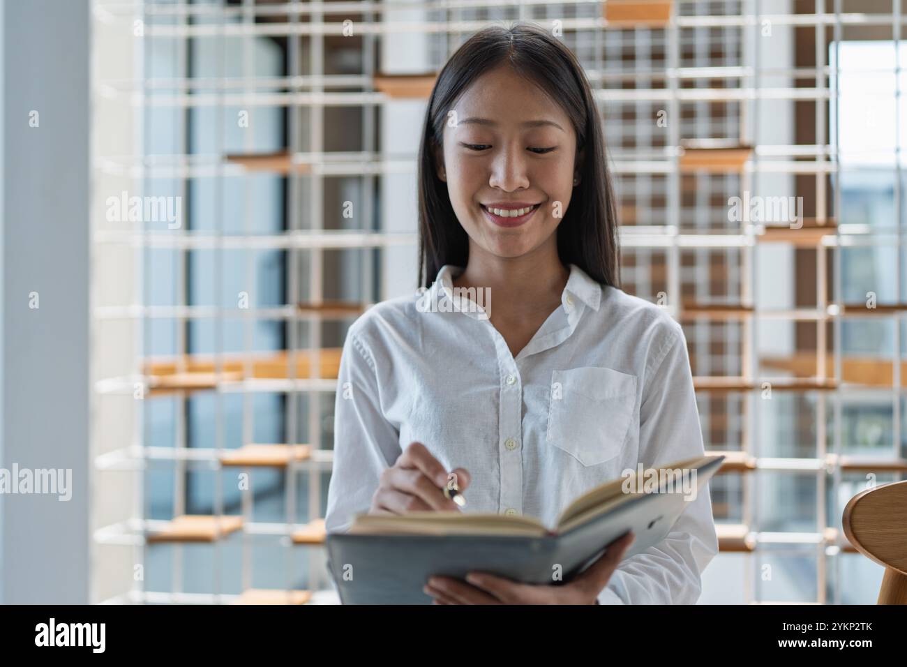 A young woman engages with a book in a bright, stylish indoor setting, reflecting concentration ...