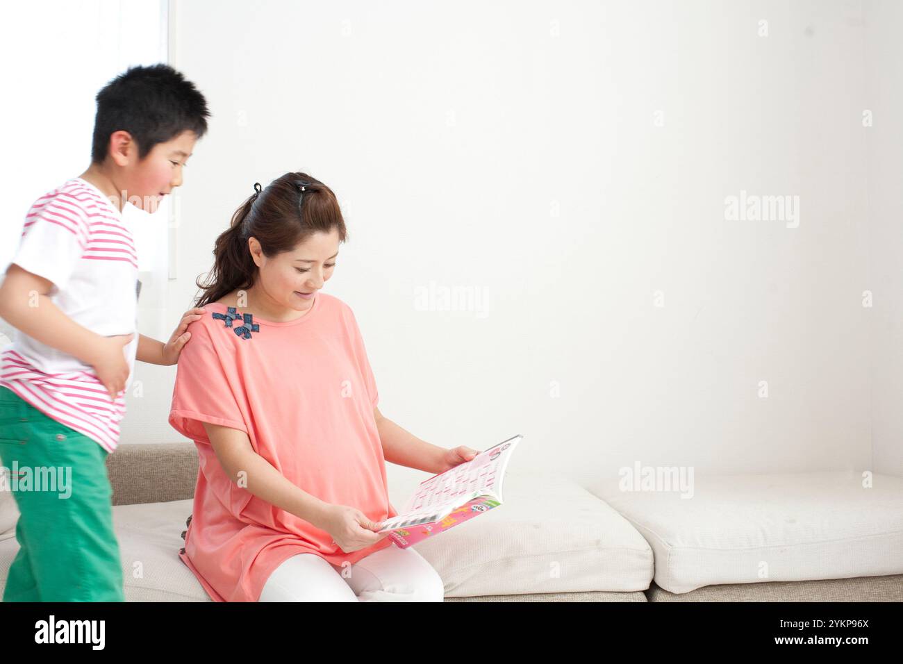 Boy cuddling up to his pregnant mother and looking at a magazine ...