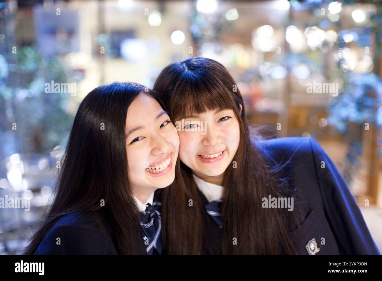Two high school girls sitting cheek to cheek in front of a café after ...
