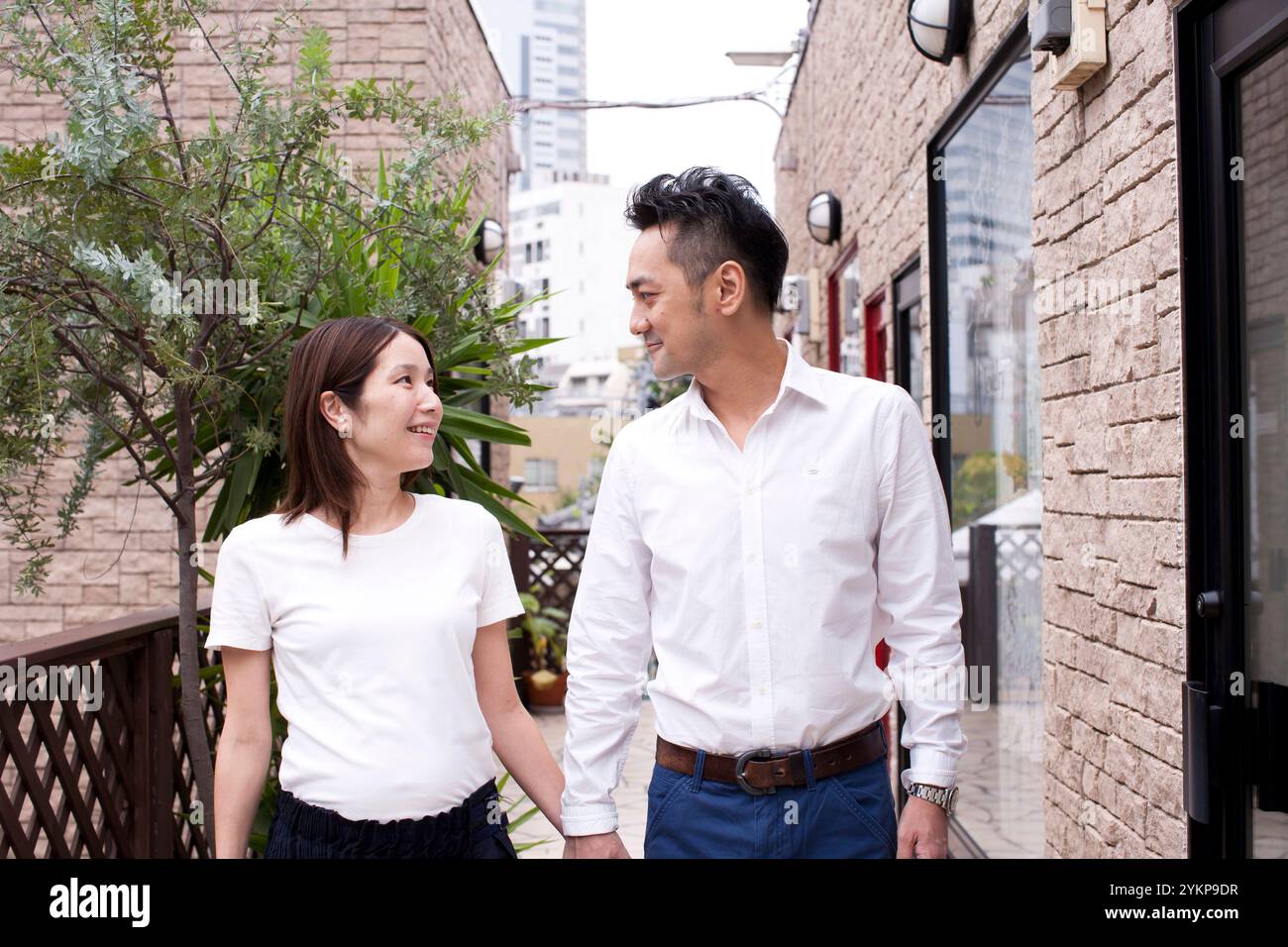 Newlyweds, a smiling pregnant wife and her husband holding hands side by side on the terrace ...
