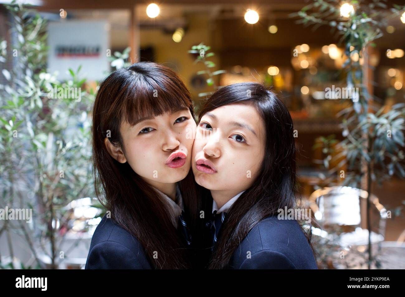 Two high school girls cheek to cheek, looking at each other and joking ...