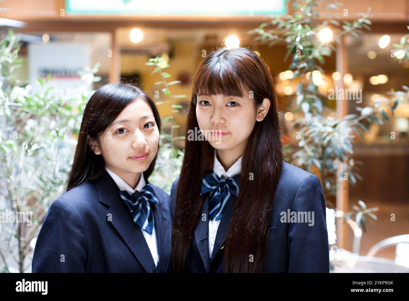 Two high school girls standing side by side in front of a café, looking ...