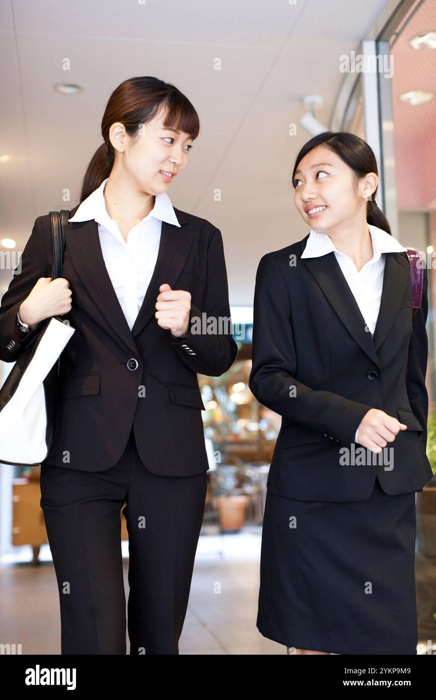 Two smiling women in suits walking in an office building having a ...