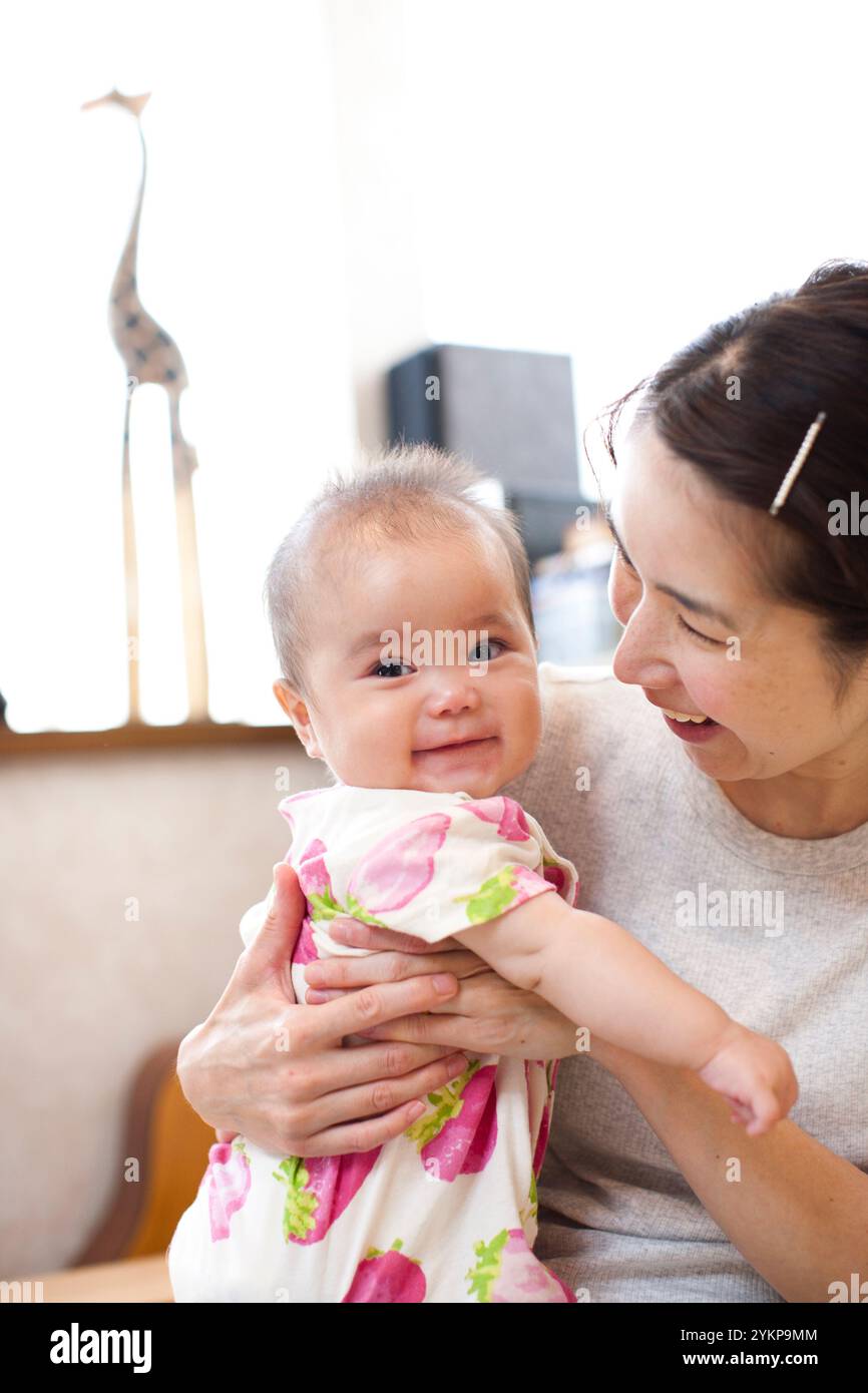Mother talking and smiling while holding her happy baby on the sofa in ...