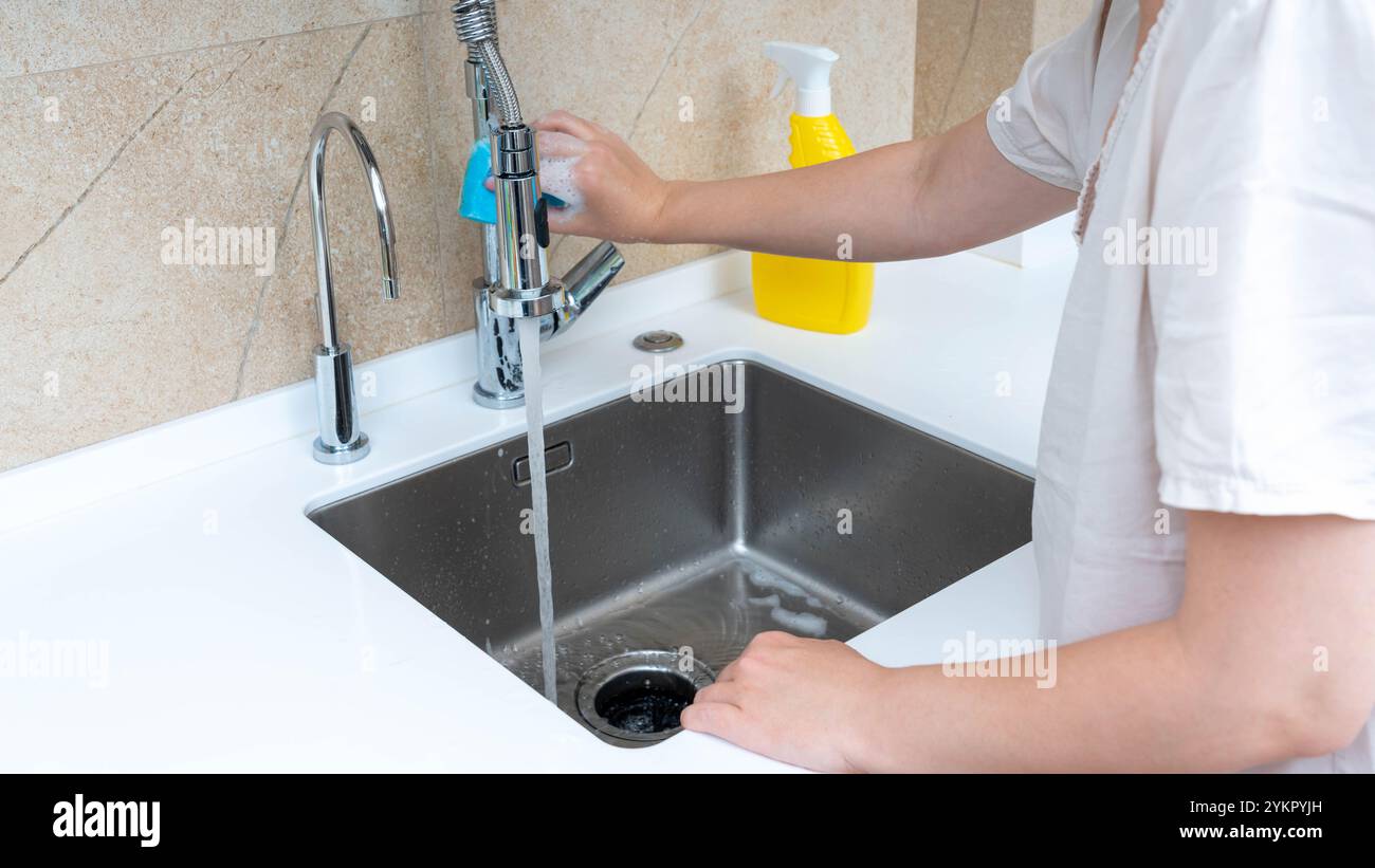 A person rinsing a blue sponge under running water using a flexible ...