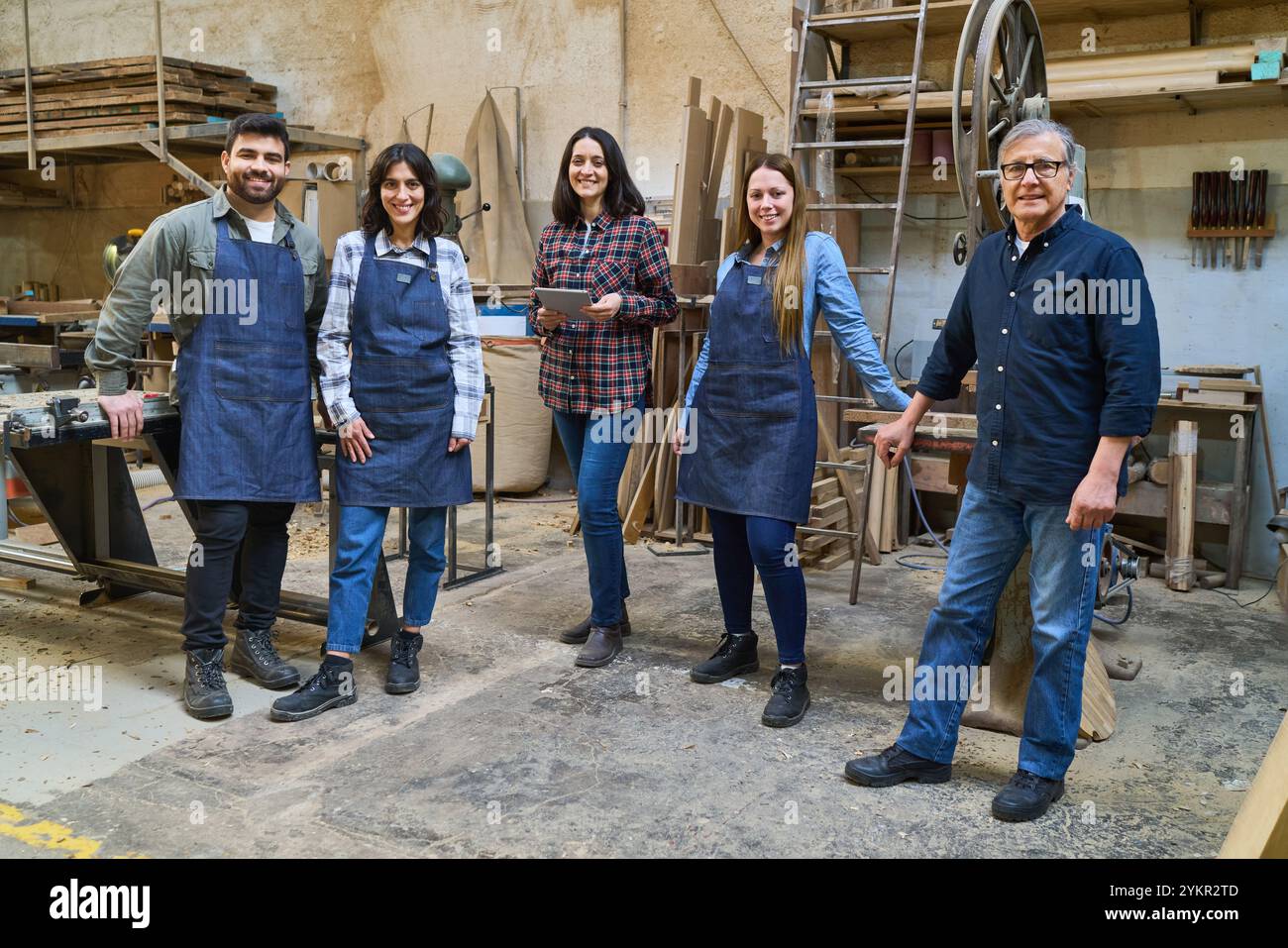 A diverse group of men and women in a lumberyard wearing aprons and ...