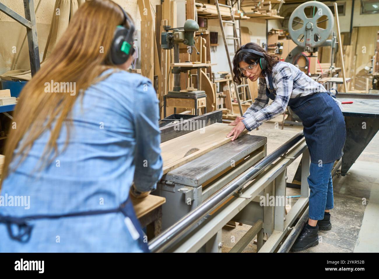 Two young apprentices work together in a busy lumberyard, learning ...