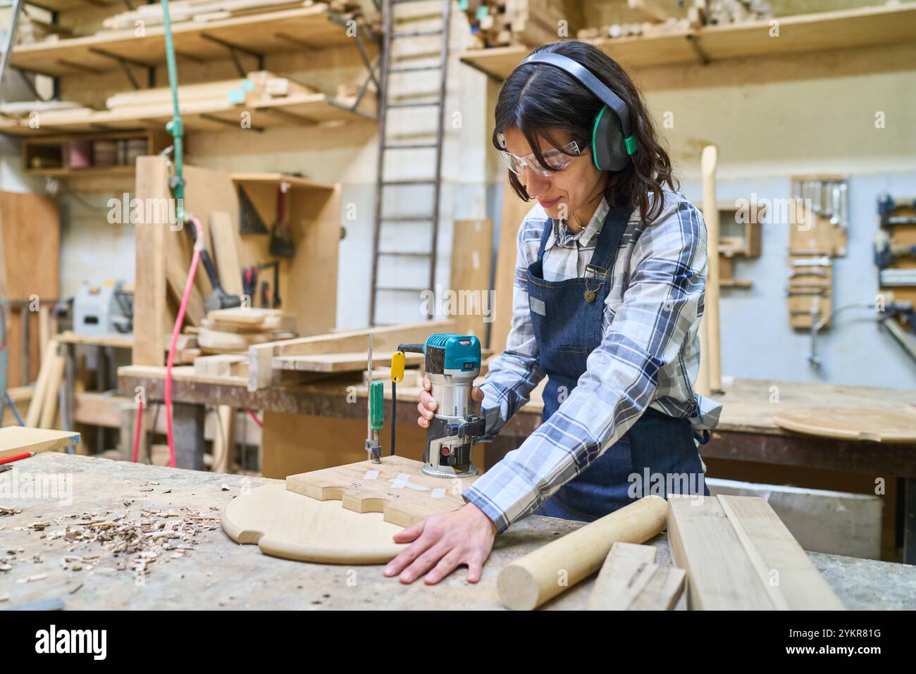 A focused worker using a router on a wooden piece in a bustling ...