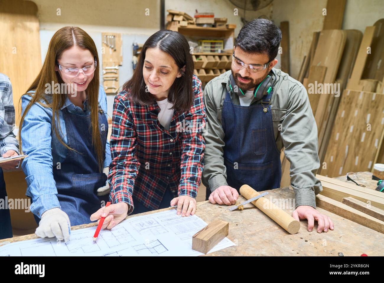 Three people collaborate on a woodworking project in a lumberyard. A ...