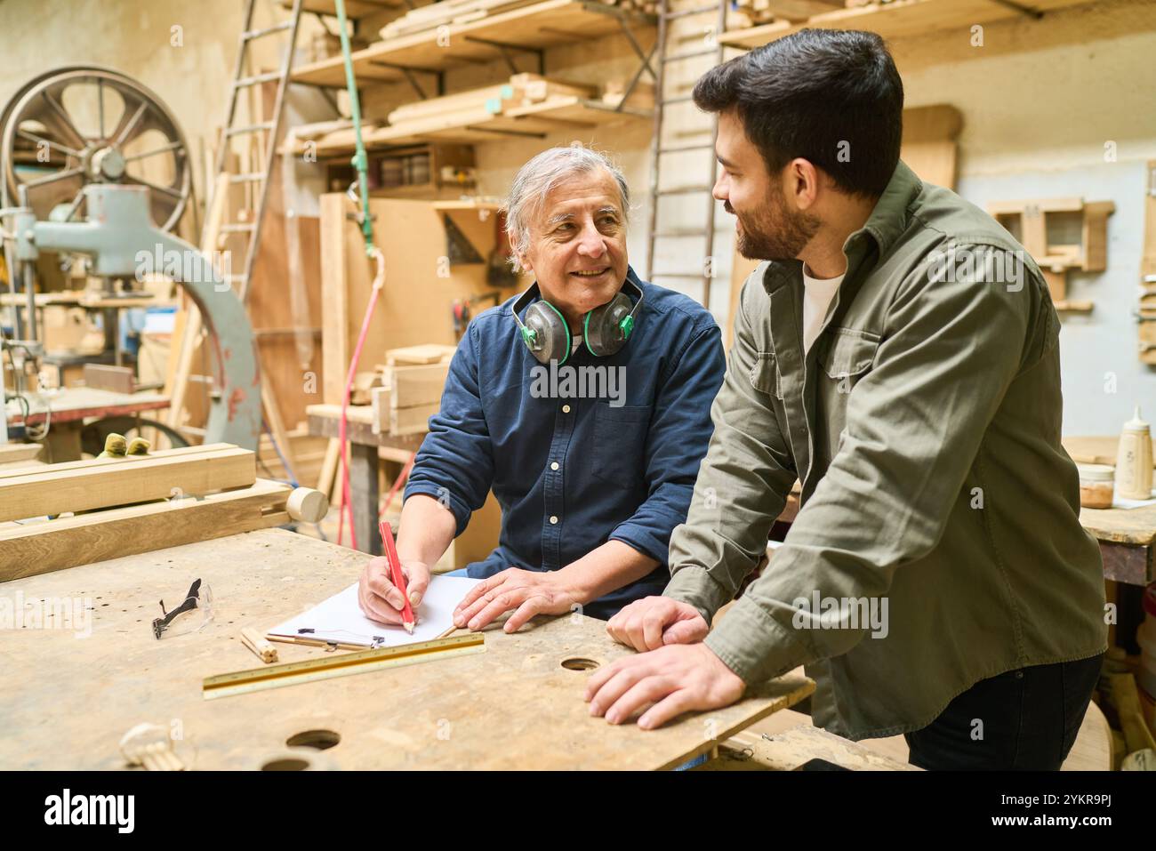 An older craftsman providing guidance to a young apprentice in a lumberyard setting, emphasizing ...