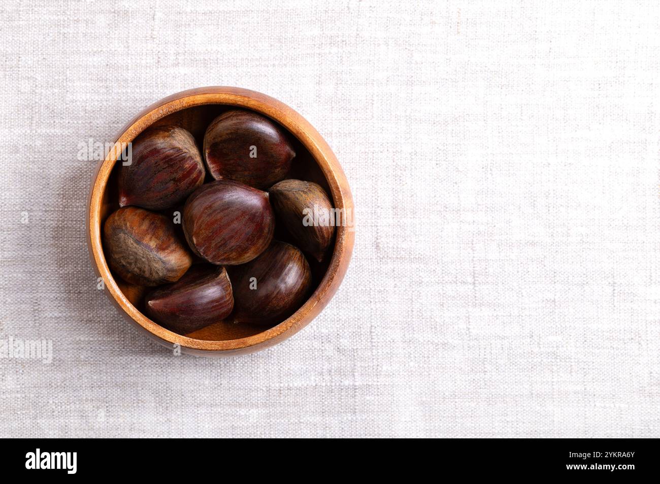 Sweet chestnuts in a wooden bowl on linen, from above, with empty space ...