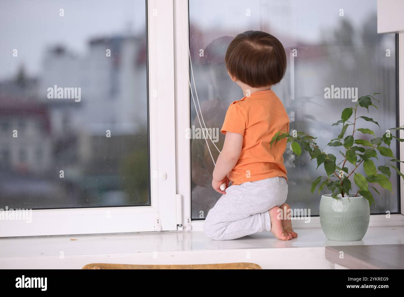 Little boy near window on windowsill, back view. Dangerous situation ...