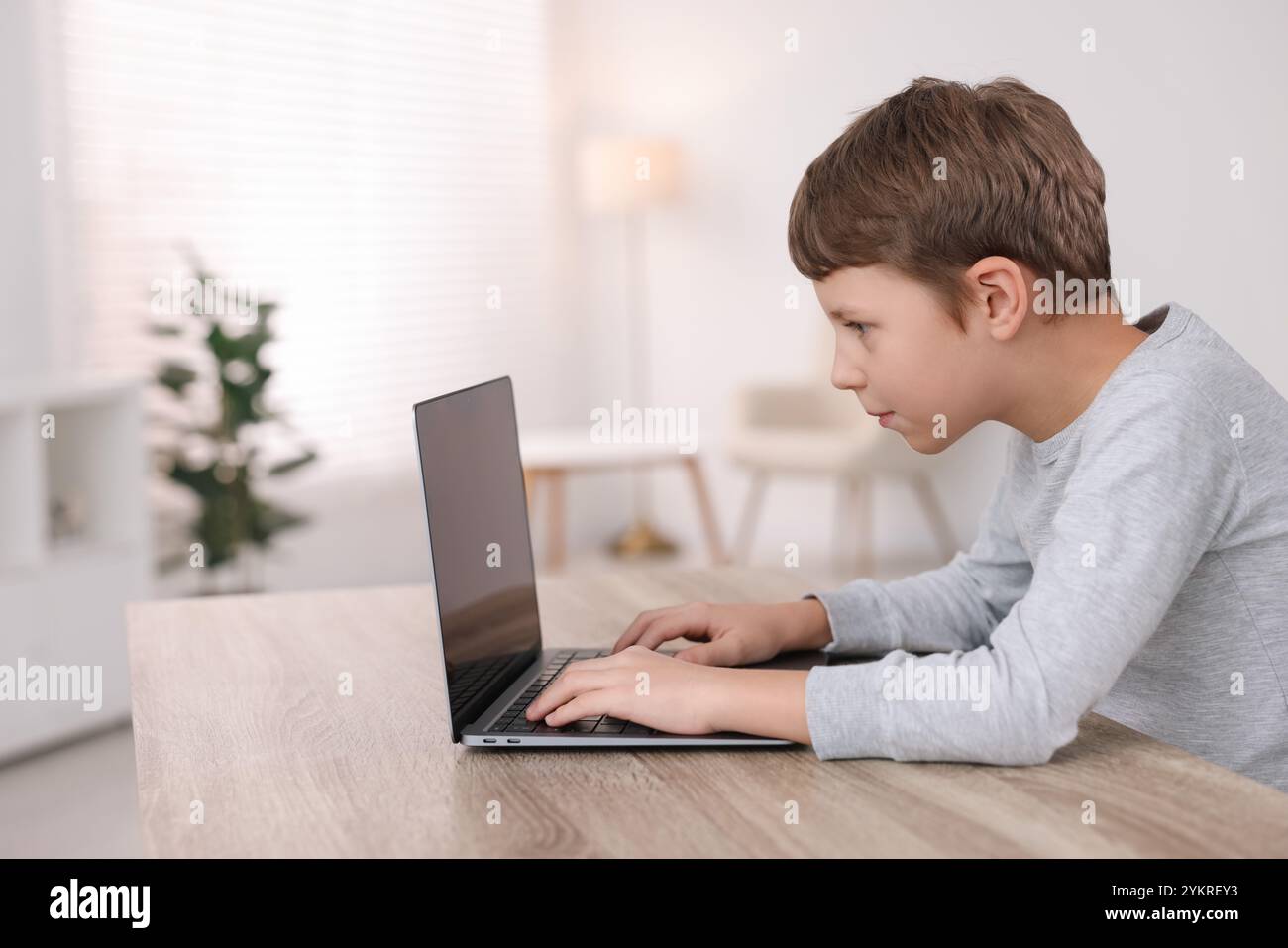 Boy with incorrect posture using laptop at wooden desk indoors Stock ...