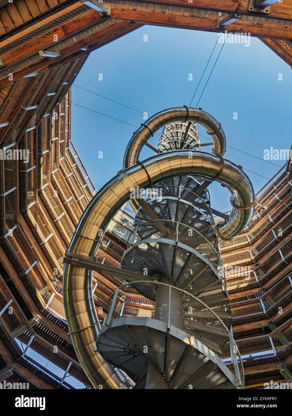 A towering spiral staircase with a metal slide winds upwards inside a ...