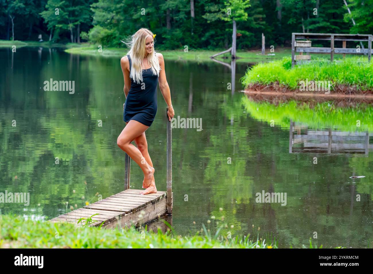 A beautiful blonde woman in a black dress poses gracefully by a serene ...