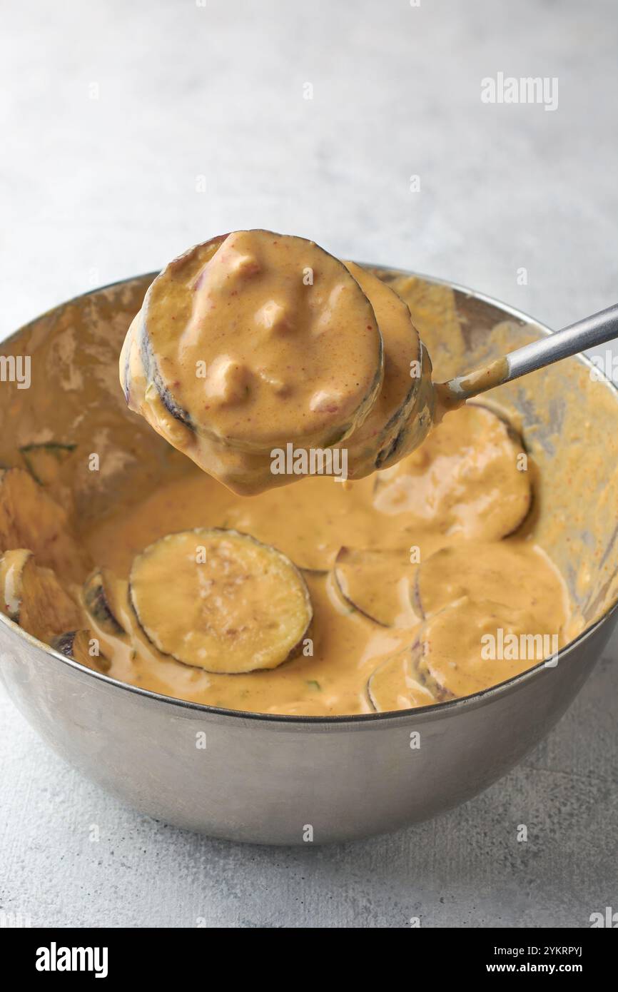 cup of sliced eggplant mixed with batter for frying with spoon white ...