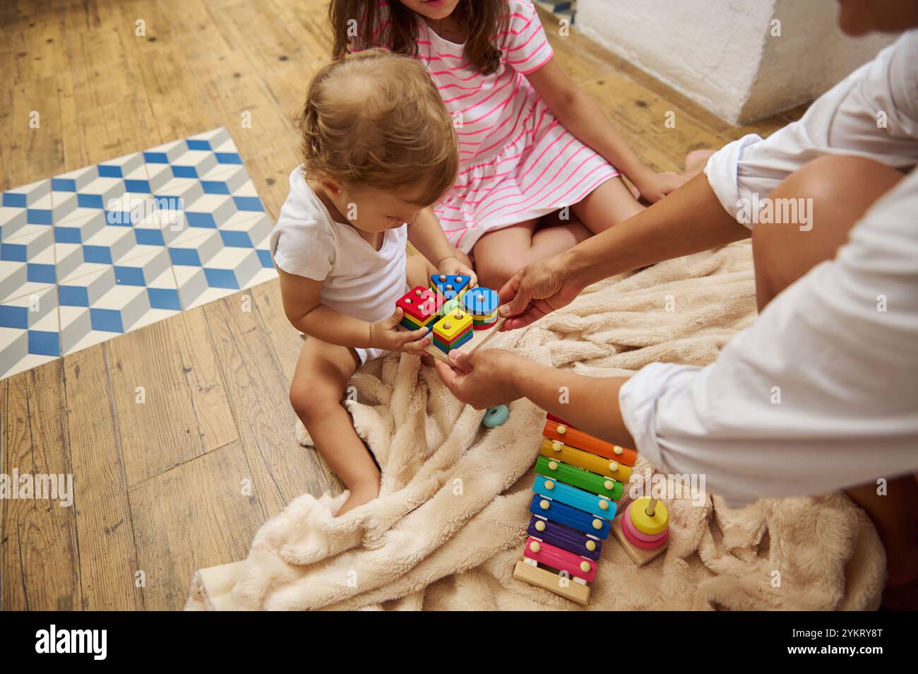 A mother and her children play happily on the floor with vibrant wooden ...