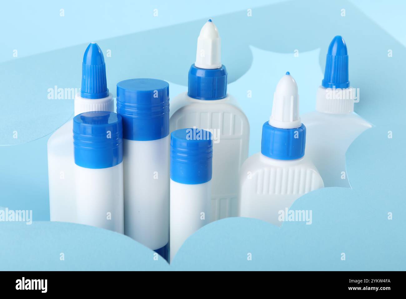 Different types of glue and paper cutout on light blue background ...