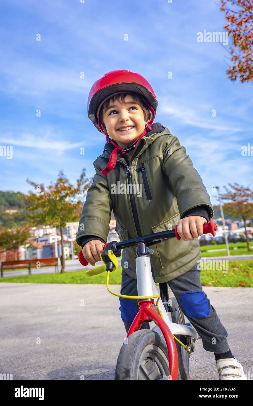 A young boy is riding a bike with a red helmet on. He is smiling and he ...