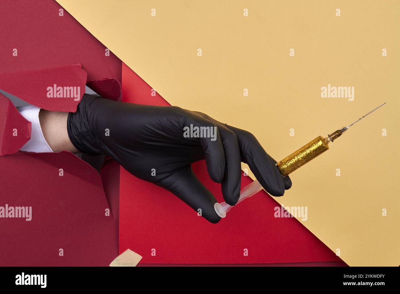 Close up hand holding syringe with yellow glitter. Red and yellow paper ...