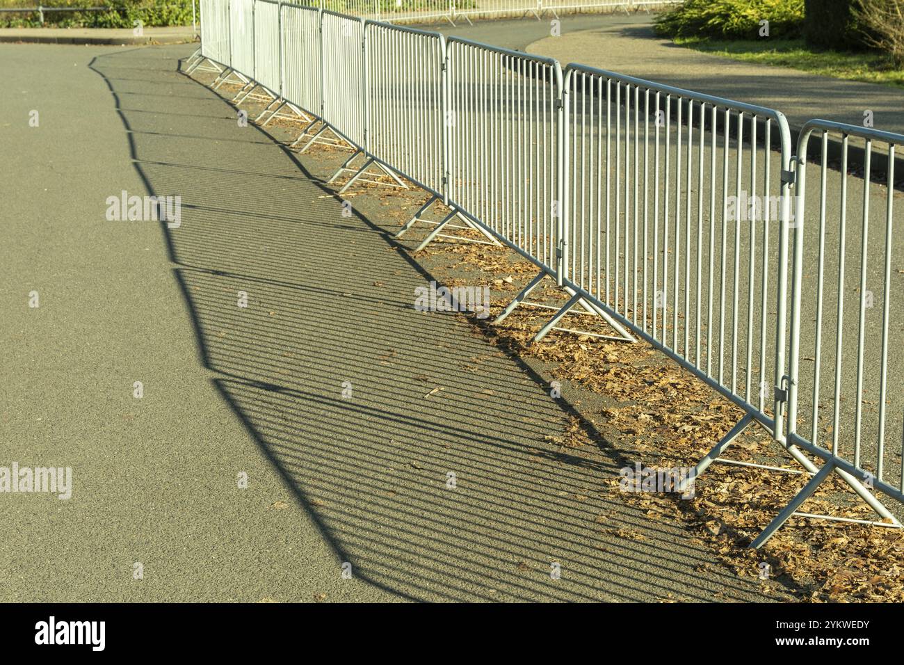 Metal crowd control barriers casting long shadows on an asphalt road ...