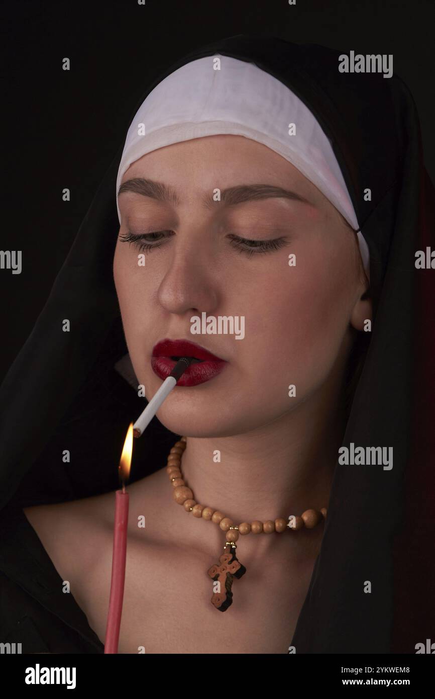 Portrait of a bad young nun lights up a cirarette using a church candle ...
