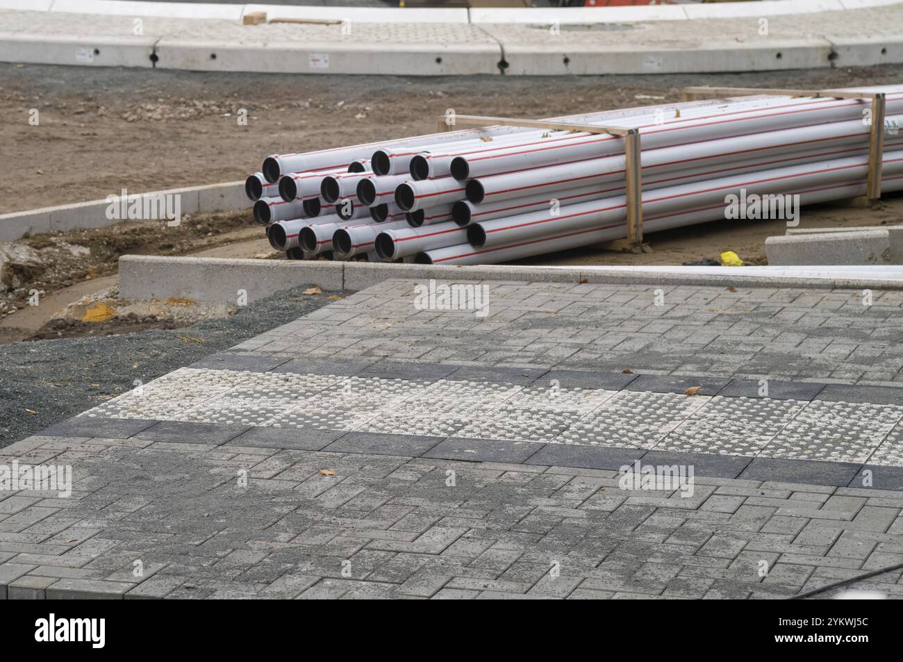 Tactile paving, stacked pipes and dirt road at construction site during ...