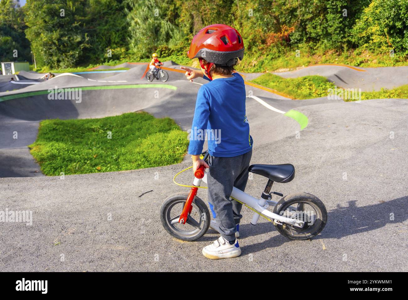 A young boy in a red helmet rides a bicycle on a paved surface. The boy ...