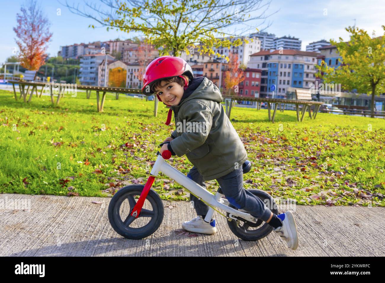 A young boy is riding a bicycle down a sidewalk. He is wearing a helmet ...
