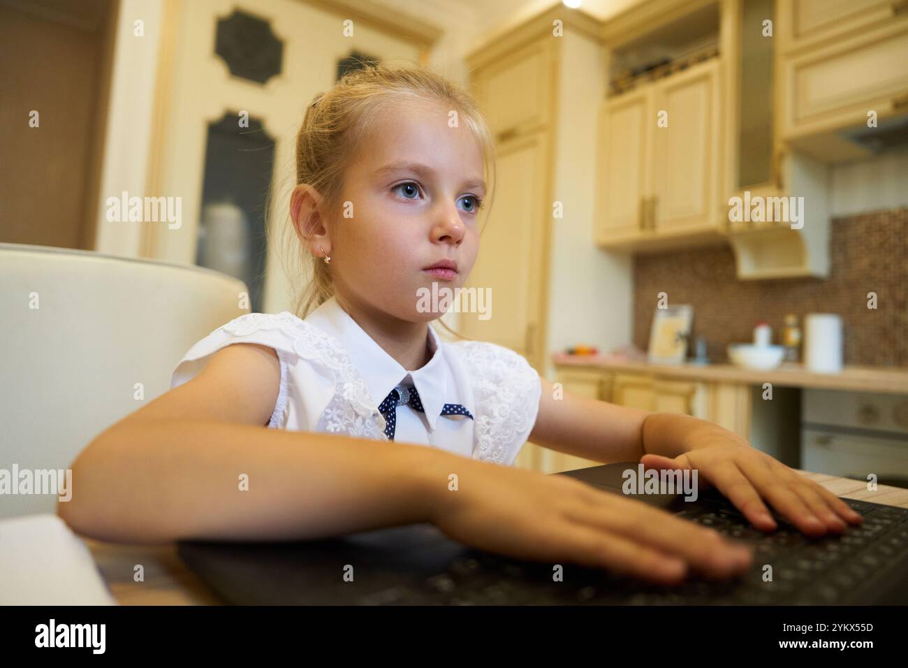 Young girl concentrating while typing on a laptop in a cozy kitchen ...
