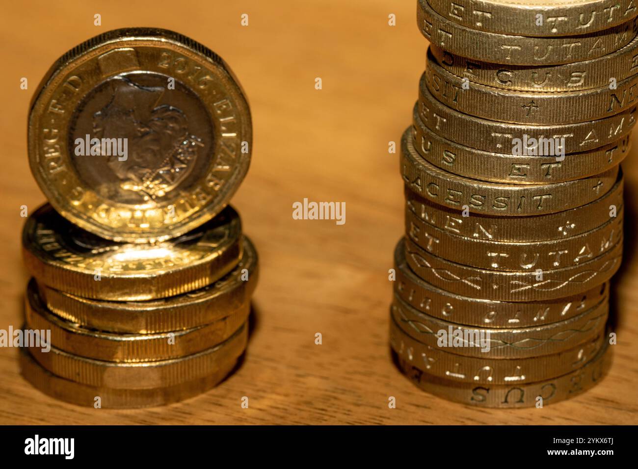 Two stacks of British one-pound coins on a wood surface. One stack is ...