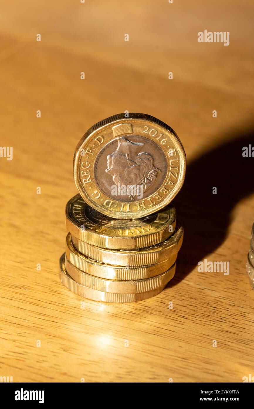 A close-up shot of a stack of British one-pound coins on a light brown ...