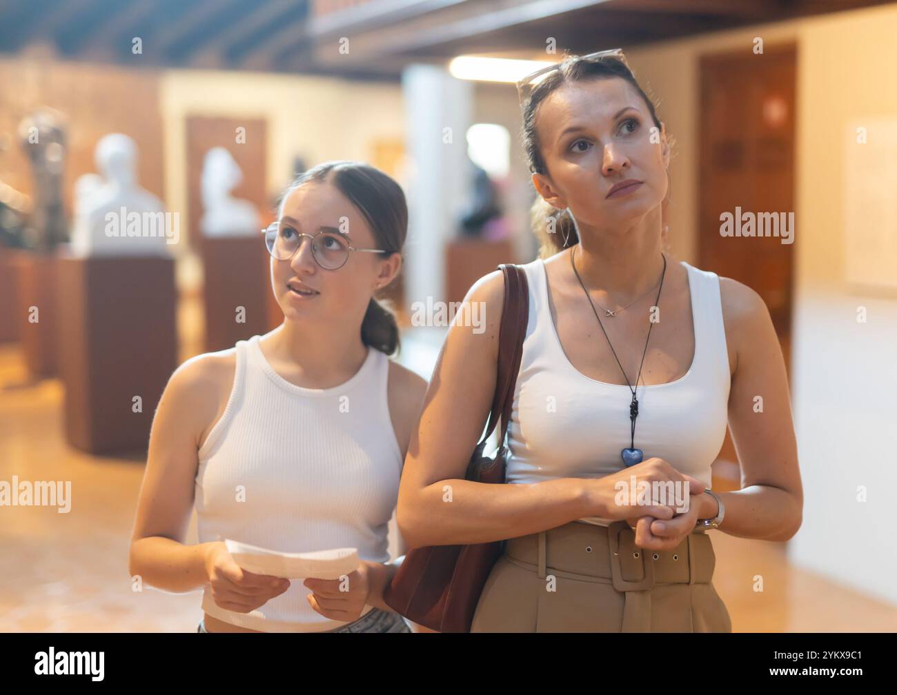 Young woman with teen daughter walk around museum, view sculpture in ...