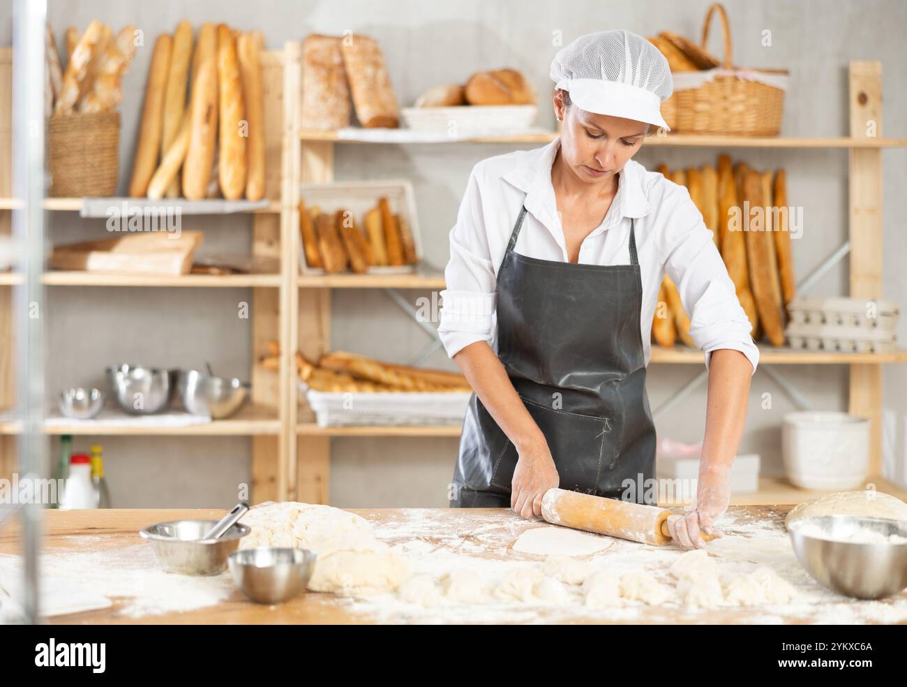 Female baker works with rolling pin, rolls out and spreads out pieces ...