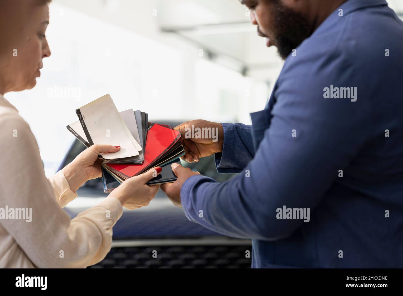 Salesperson in auto showroom discussing with man, offering color swatch ...