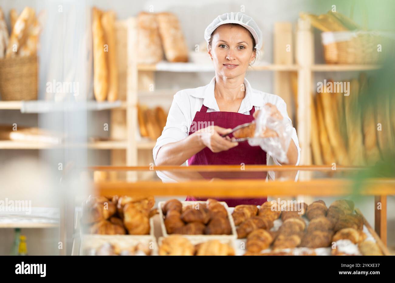 Positive female bakery seller with tongs in his hands offers to buy ...