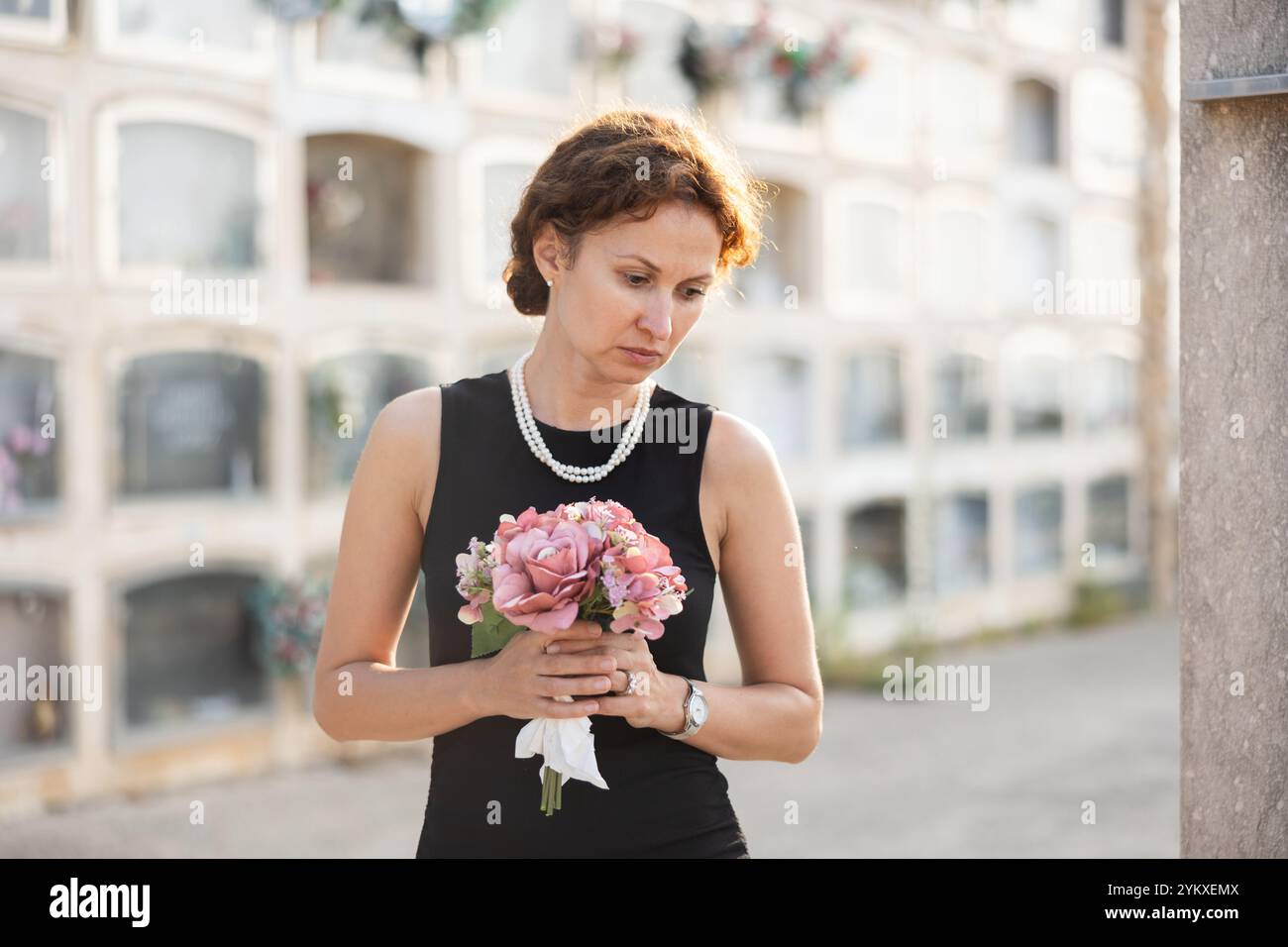 Woman in black mourning dress standing with flowers near columbarium ...