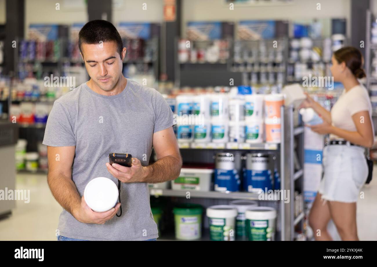 Focused man scanning barcode on paint can in construction hypermarket ...