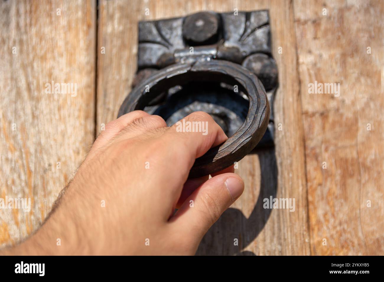 Male hand knocking with an old black iron knocker on a rustic wooden ...