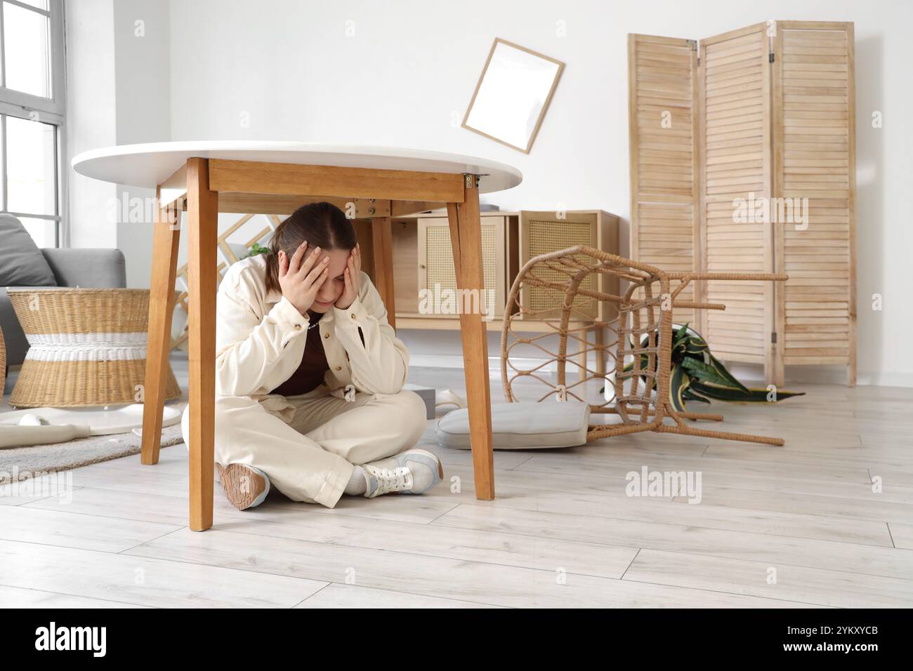 Young woman hiding under table in living room during earthquake Stock ...
