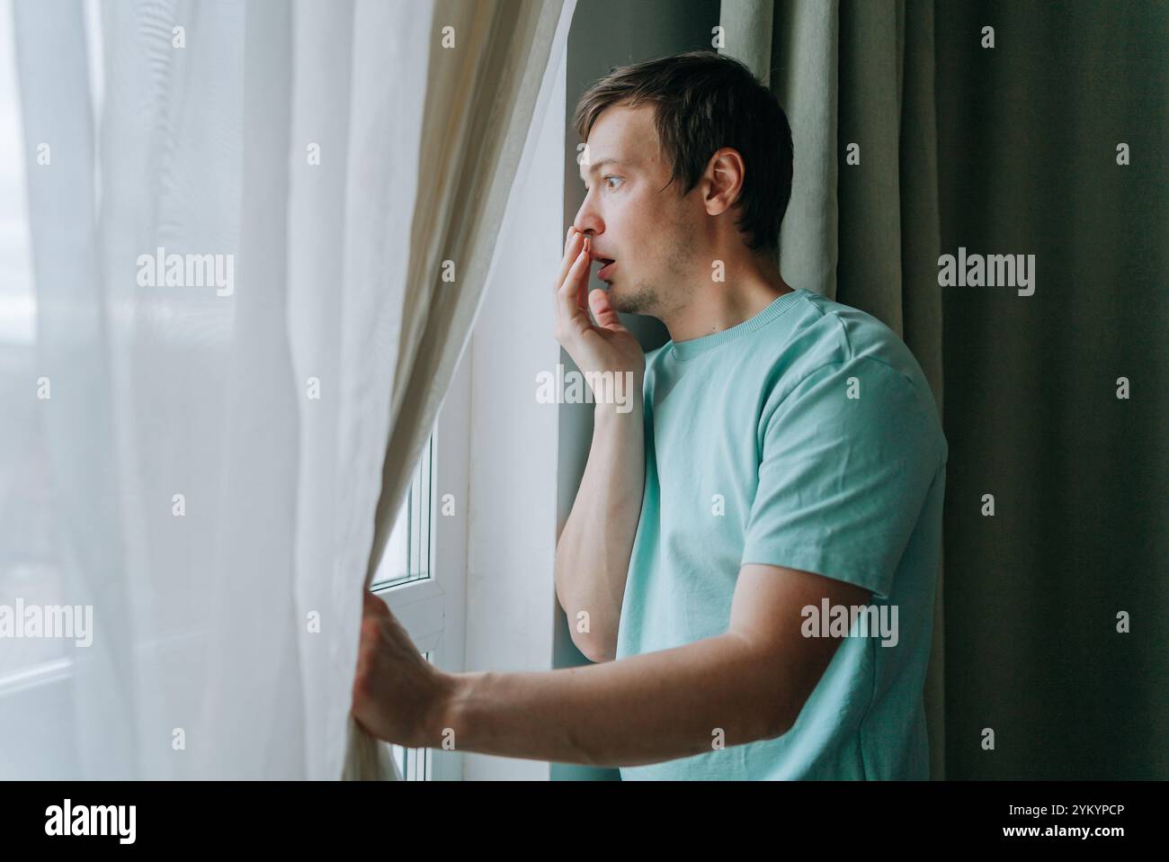 Shocked man is peeking out the window from behind curtain, covering his ...