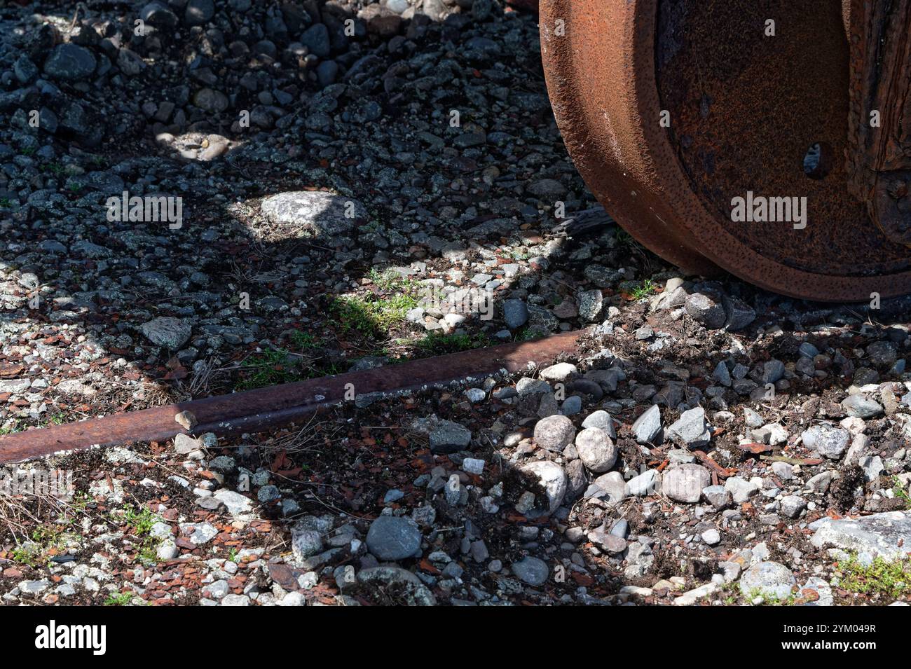 An old train wheel sits on an old rail. It is brown with rust. It looks ...