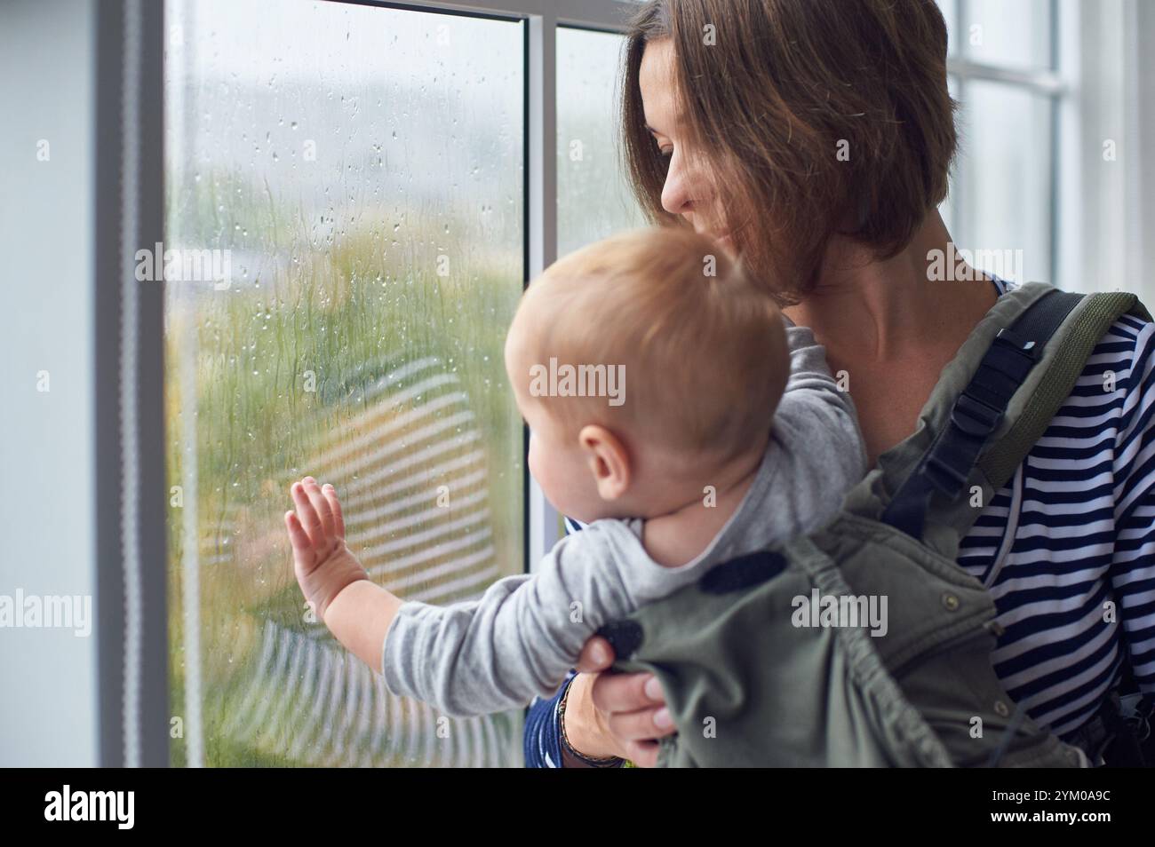 Mother and child observe rain through window on a cozy day indoors ...