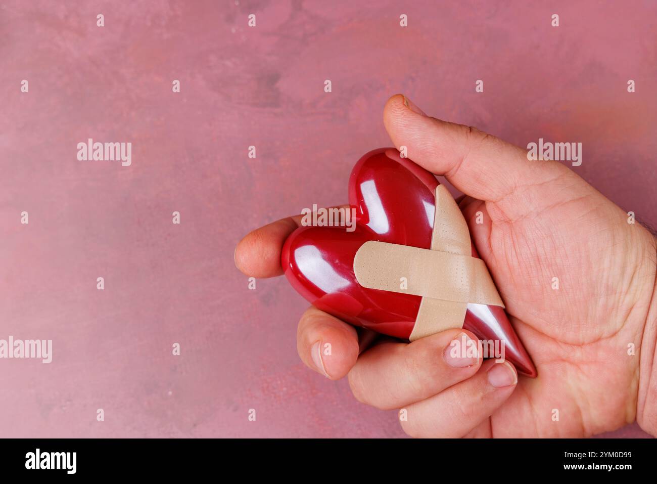 A detailed view of a hand holding a red ceramic heart with crossed ...