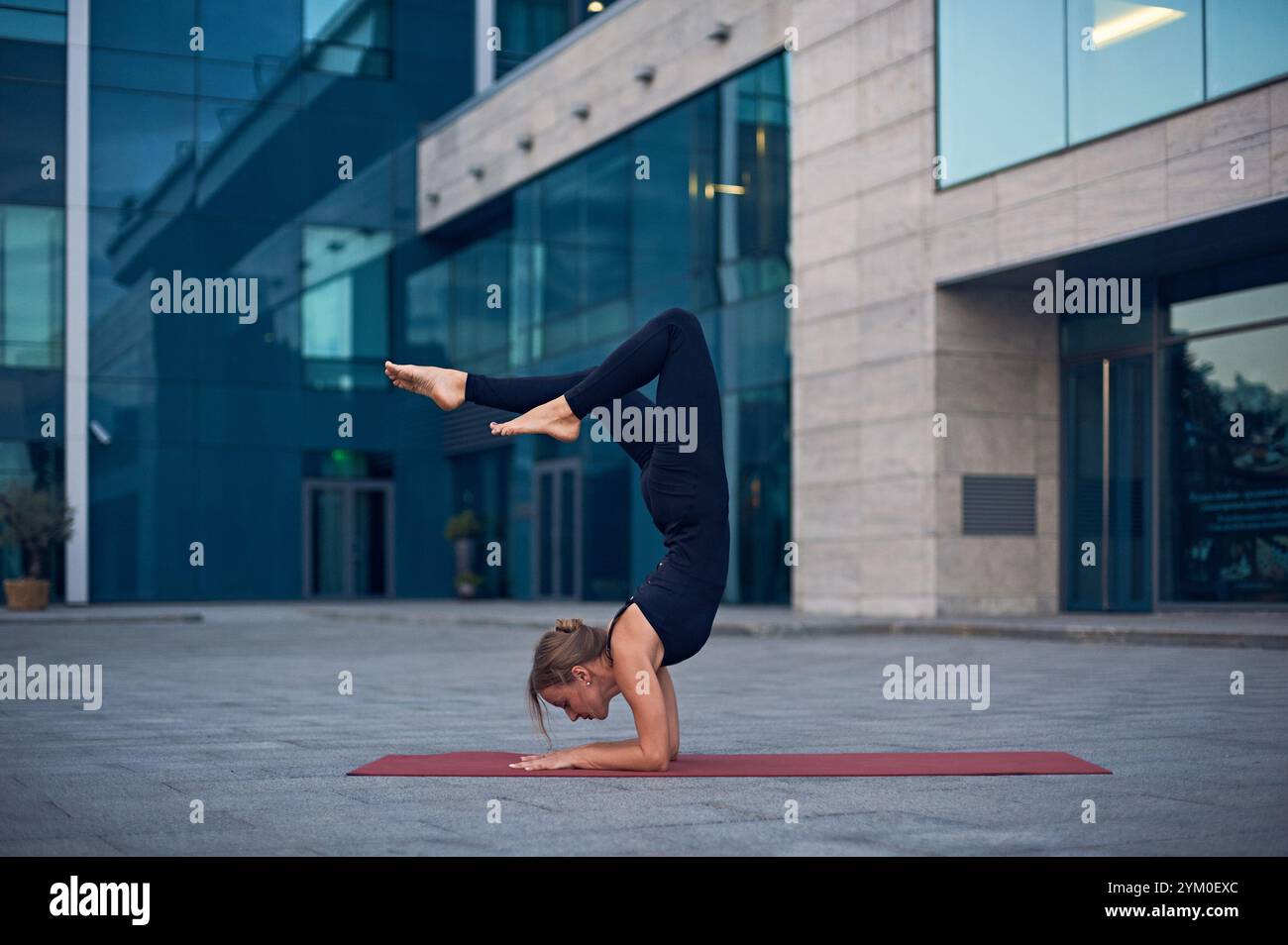 Yoga practitioner demonstrates advanced pose on red mat outdoors at ...