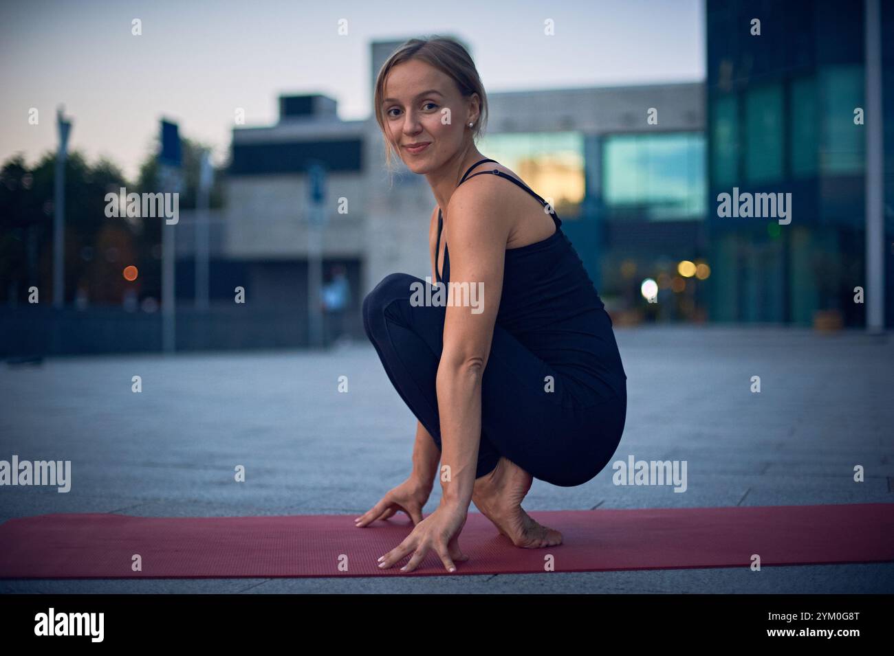 Yoga practitioner demonstrates squatting pose at urban plaza during ...