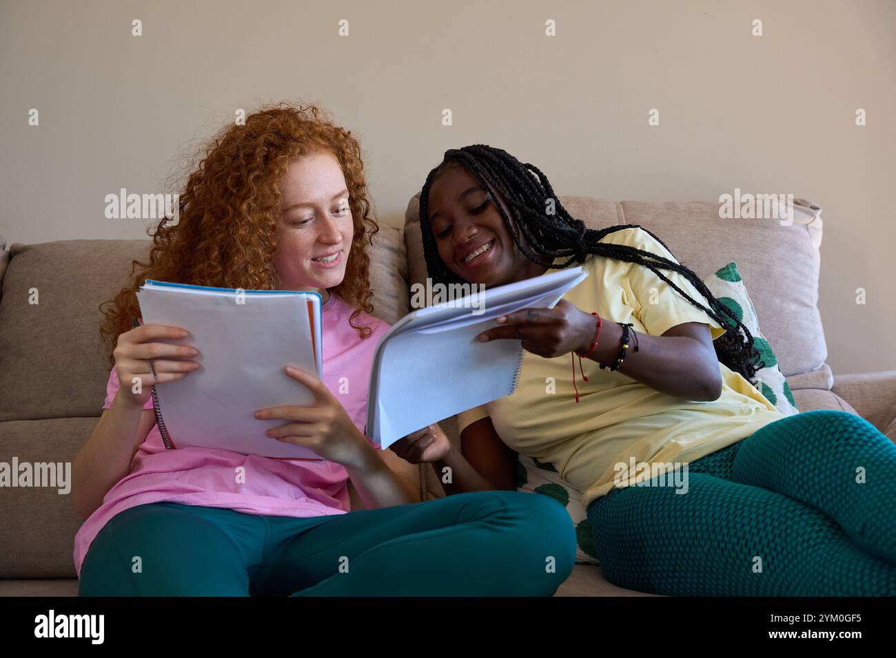 Two female students studying and comparing notes on sofa at home Stock ...