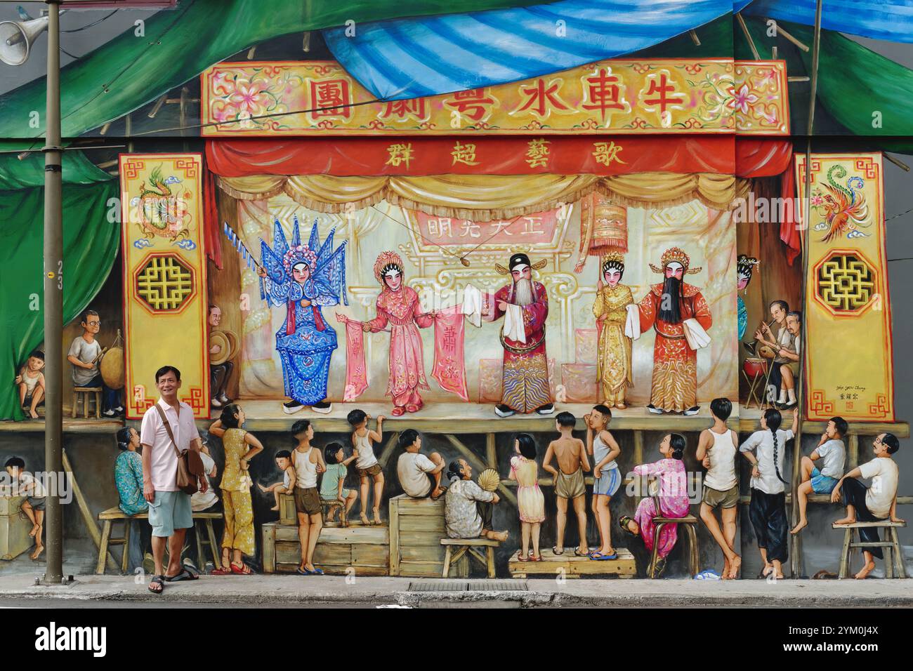 A man poses in front of a mural by Yip Yew Chong depicting a Cantonese opera performance of ...