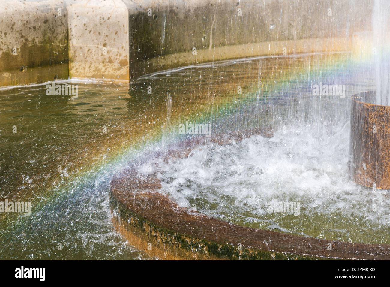 A vibrant rainbow forms over splashing water in a fountain Stock Photo ...
